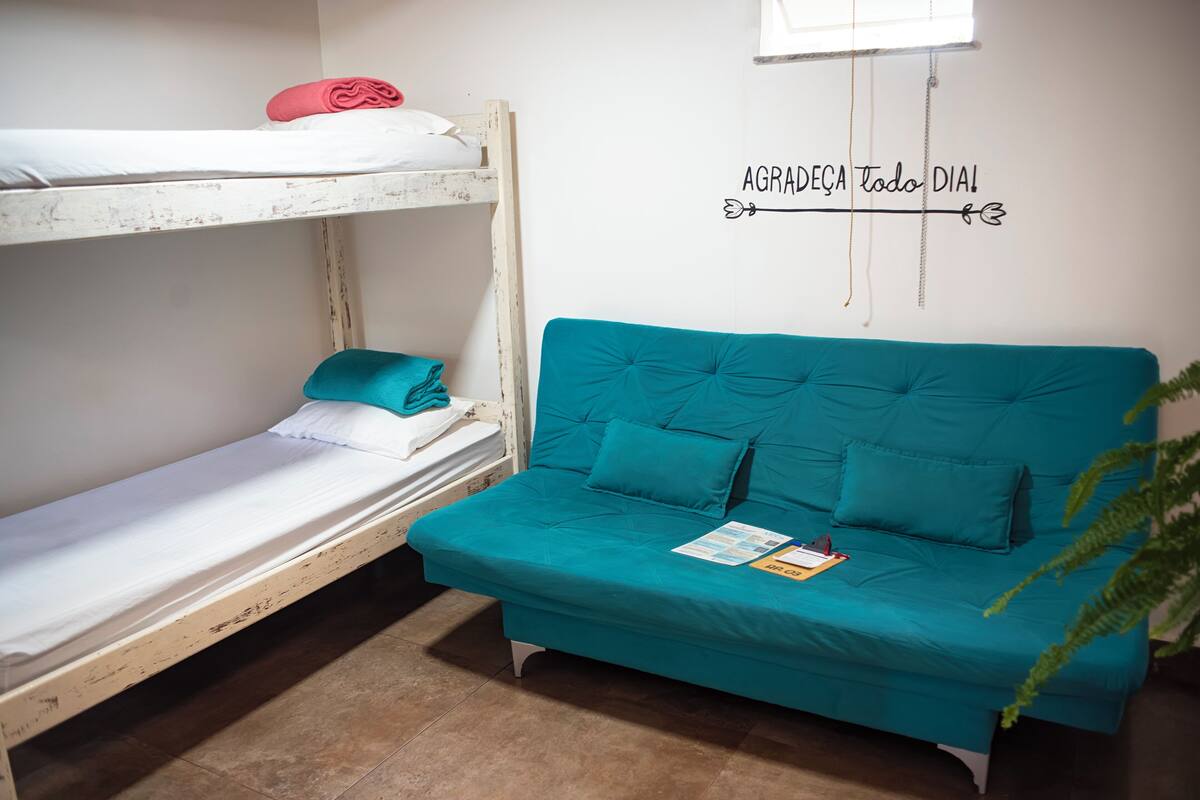 Quarto em dormitório com beliches e um sofá verde-água.