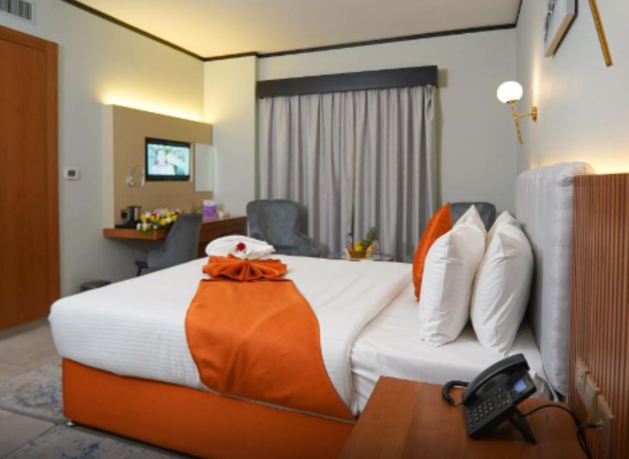 Quarto de hotel com cama, escrivaninha com telefone, cadeira, televisão e cortina.