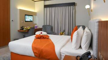 Quarto de hotel com cama, escrivaninha com telefone, cadeira, televisão e cortina.