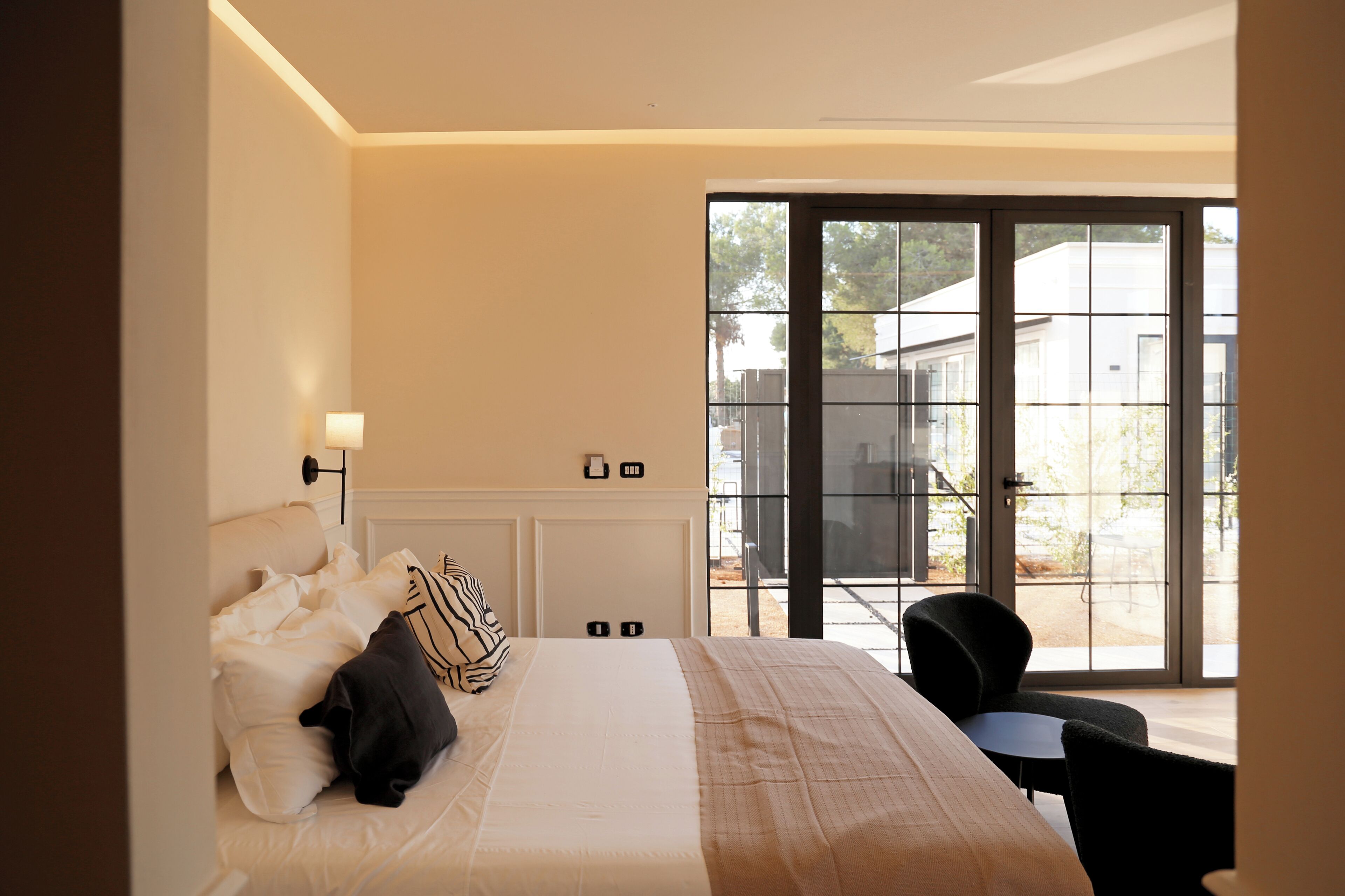 Quarto de hotel com uma cama, uma cadeira e vista para o exterior através de uma porta de vidro.