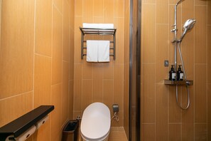 Uma casa de banho moderna com sanita, porta-toalhas, chuveiro e um cesto de lixo.