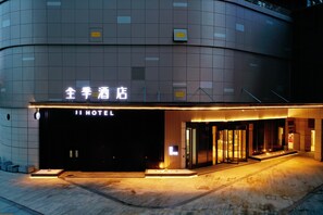 Entrada de hotel com design moderno, destacando uma placa e fachada bem iluminada.