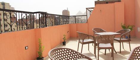 Terraço no telhado com mesa e cadeiras, plantas em vasos e um portão decorativo.