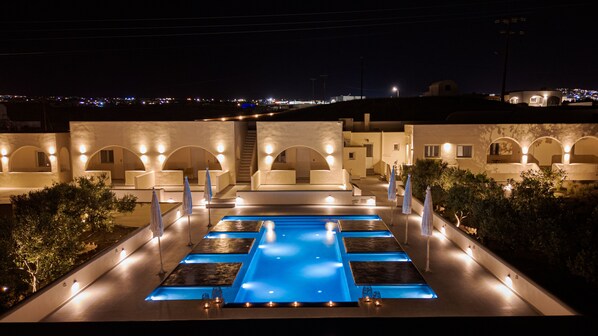 Uma área de piscina com várias piscinas, um espaço coberto para descanso e vista da cidade à noite.