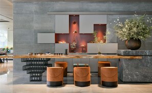 Uma área de bar moderna com bancada de mármore, banquetes e plantas decorativas.