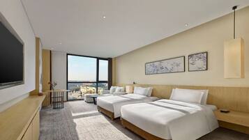 Quarto de hotel moderno com duas camas, uma janela ampla e vista para a cidade.