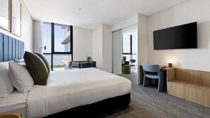 Quarto de hotel moderno com uma cama grande, uma escrivaninha, uma cadeira e uma televisão na parede.