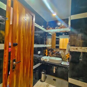 Um banheiro com porta de madeira, pia com produtos de higiene, espelho e painel de backsplash em mármore.
