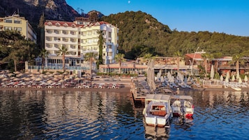 Um hotel à beira-mar com várias varandas, uma área de praia com espreguiçadeiras e uma marina com barcos.