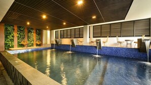 Piscina interna com borda azulejada, teto de madeira e área de estar com cadeiras.