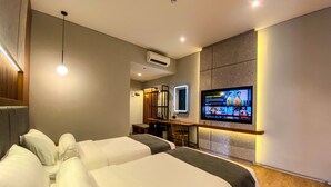 Quarto de hotel com duas camas, TV fixada na parede, escrivaninha e área de estar com cadeiras.