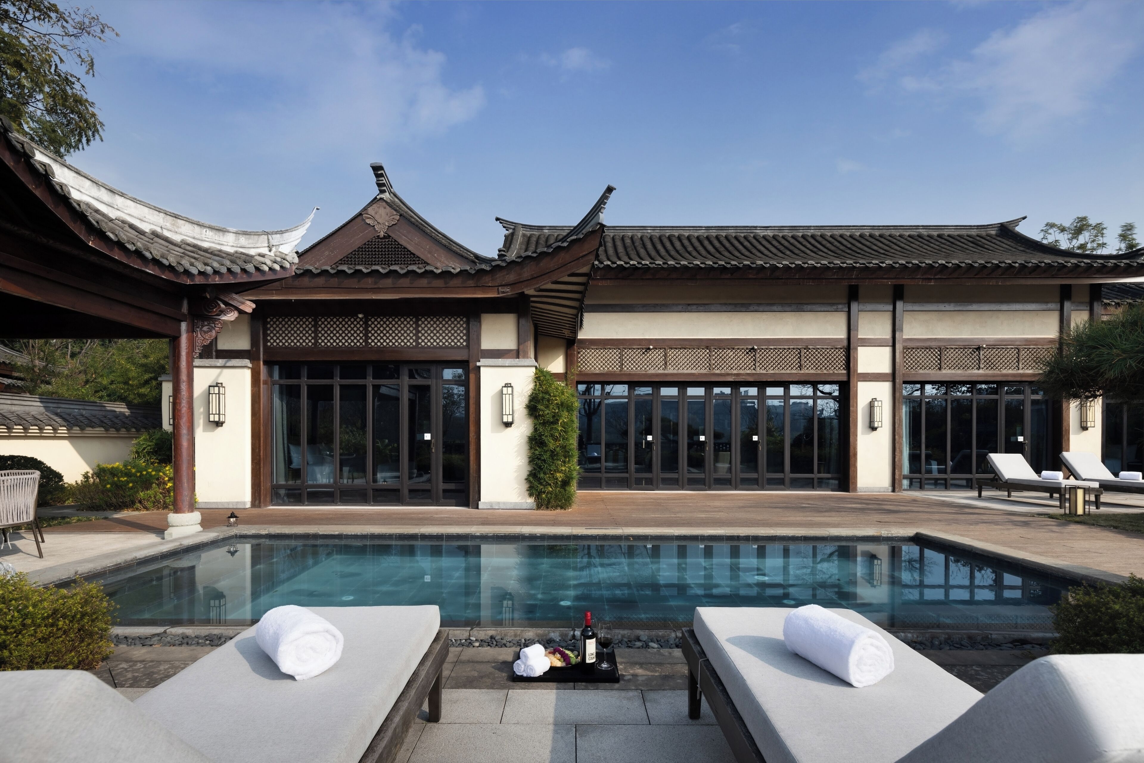 Um edifício tradicional com área de piscina, espreguiçadeiras e uma bandeja com garrafa e copo.