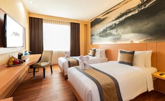 Quarto de hotel com duas camas, uma escrivaninha com cadeira, televisão e um quadro de uma paisagem.