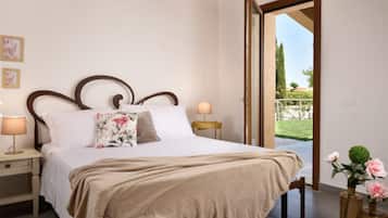 Quarto com cama, abajures, cabeceira de madeira, janela com vista para o verde e porta que dá para o exterior.