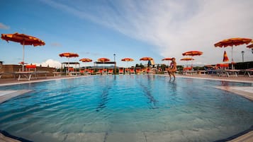 Piscina com vários espreguiçadeiras e guarda-sóis, rodeada por um muro de pedra e céu claro.