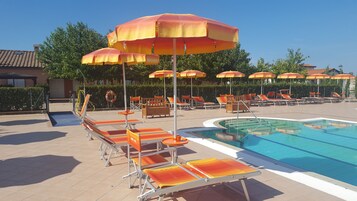 Uma área à beira da piscina com espreguiçadeiras, guarda-sóis e um salva-vidas.