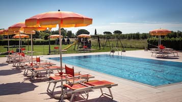 Piscina com espreguiçadeiras e guarda-sóis, cercada por uma área ajardinada.