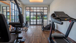 Academia com equipamentos de exercício, janelas amplas e piso de madeira.