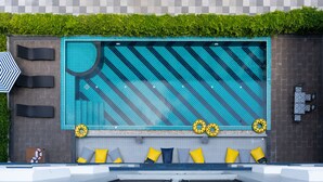 Piscina no terraço com azulejos listrados em azul e preto, almofadas amarelas e azuis e um padrão de piso xadrez.