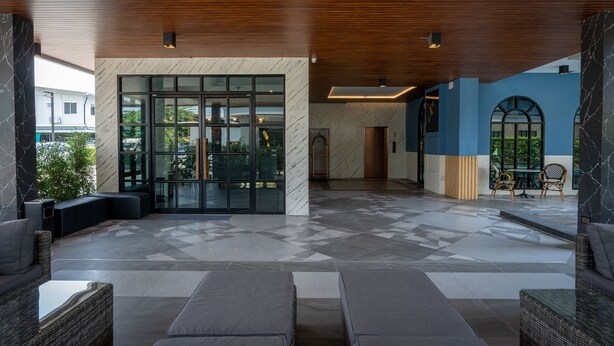 Um lobby moderno com piso de azulejos geométricos, área de estar com sofás e uma mesa, e uma grande entrada com porta de vidro.