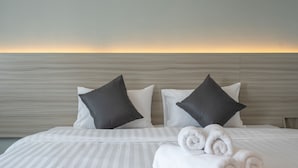 Cama bem arrumada com roupa de cama listrada e duas almofadas, uma branca e outra escura, em quarto com cabeceira de madeira e vista do céu.