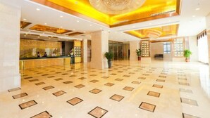 Um hall amplo com piso lustroso, um grande lustre e uma área de recepção com balcão.