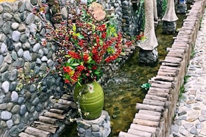 Parede de pedra com um vaso verde contendo flores vermelhas.
