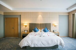 Quarto de hotel com uma cama grande, duas mesas de cabeceira, um guarda-roupa de madeira e uma porta.