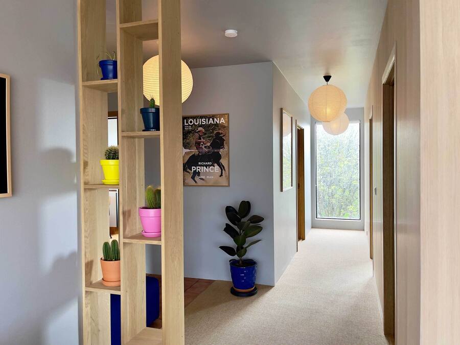 Um corredor com estante de madeira, plantas em vasos, um cartaz e uma janela ampla.