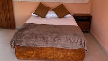 Quarto com cama grande, duas almofadas, mesa de cabeceira de madeira e janela com cortinas.
