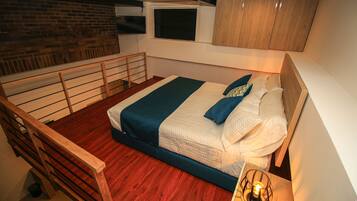Um quarto com uma cama de madeira, uma mesa de cabeceira com abajur, uma janela e uma parede de tijolos.