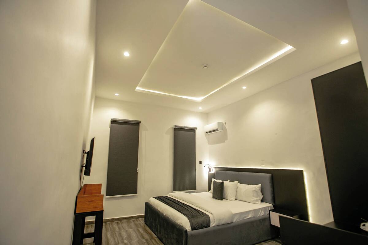 Quarto moderno com cama, mesa de cabeceira e luminária no teto.