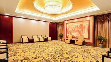 Uma sala de conferências de hotel com carpete estampado, um candelabro e uma pintura grande na parede.