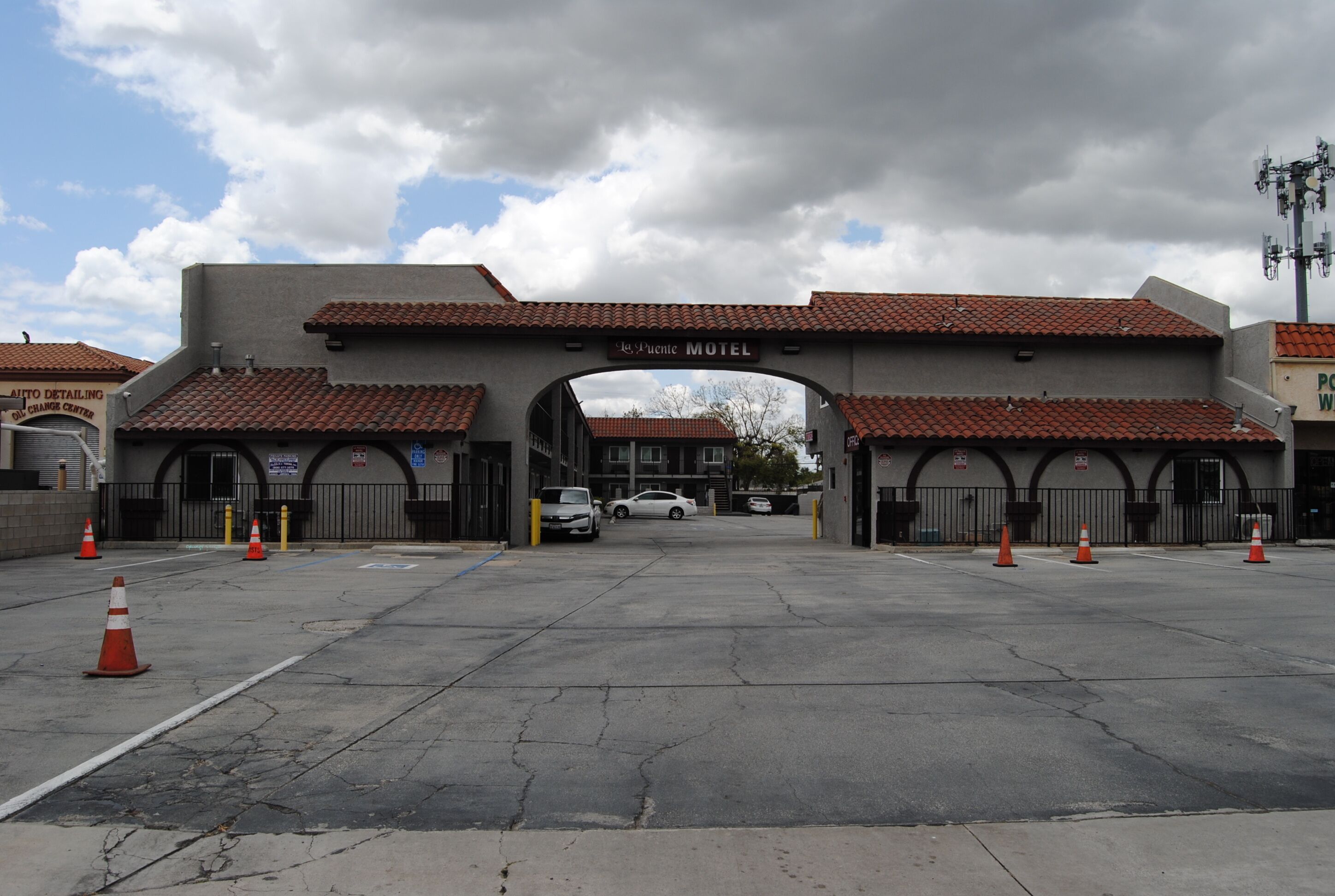 Um motel com uma grande entrada em arco, vários espaços de estacionamento e cones de trânsito laranja.