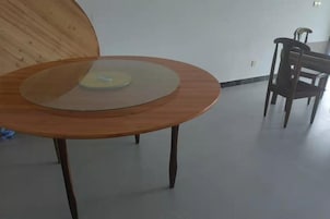 Mesa redonda de madeira com tampo de vidro, uma cadeira de madeira e uma parede branca lisa ao fundo.