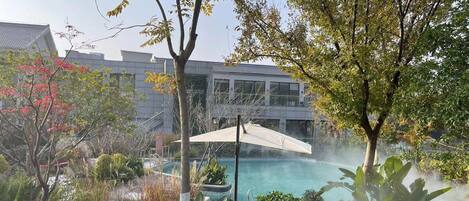 Piscina cercada por vegetação exuberante e um edifício moderno ao fundo.