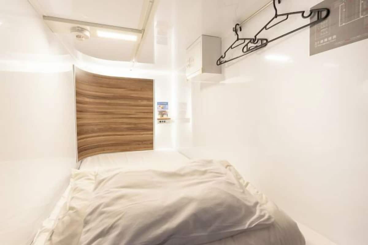 Quarto de hotel estreito, com uma cama, painel de parede em madeira e luminária fixada.