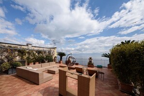 Terraço no telhado com móveis de vime, plantas em vasos e vista para o mar.