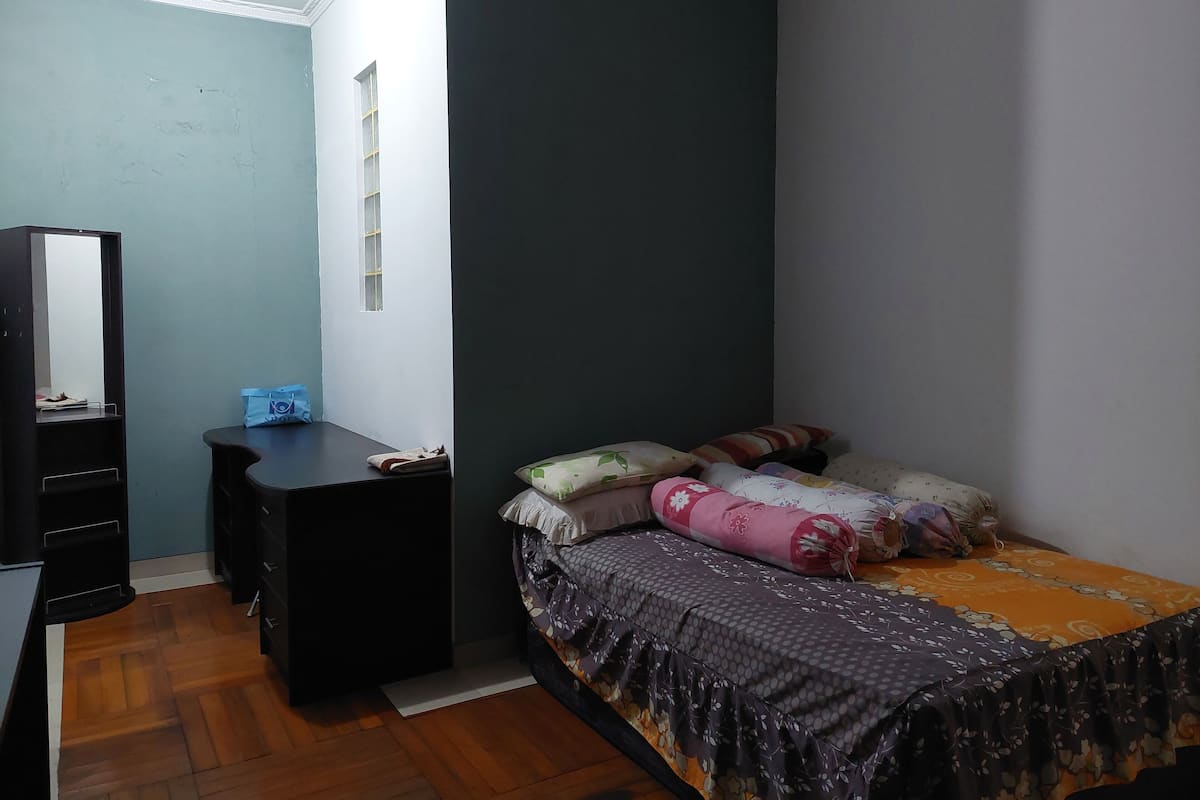 Quarto com cama, penteadeira, espelho e janela.