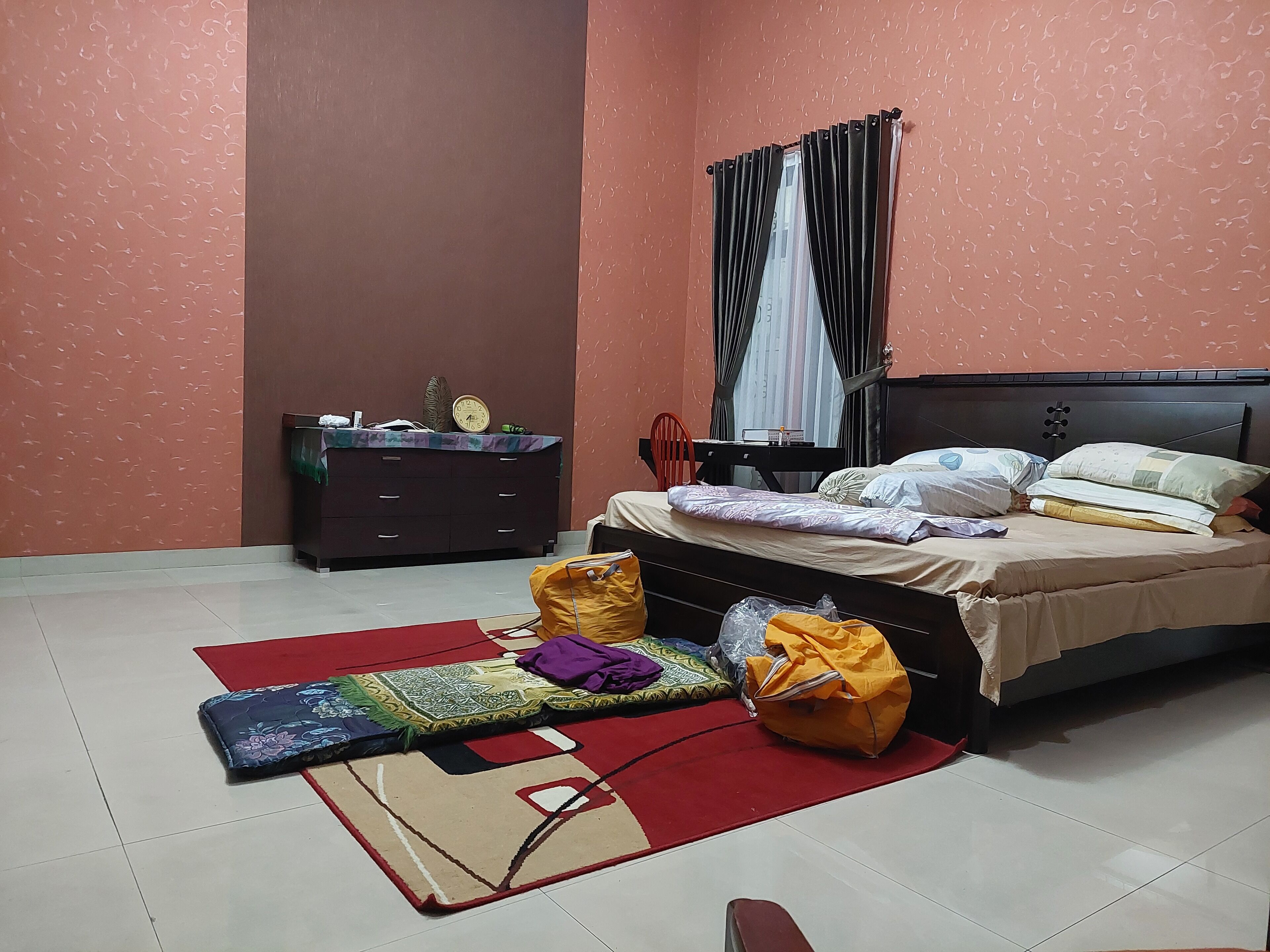 Quarto com uma cama, cômoda, relógio e janela com cortinas.