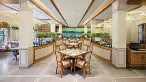 Uma ampla sala de jantar com pé direito alto, lustres e um mural central.