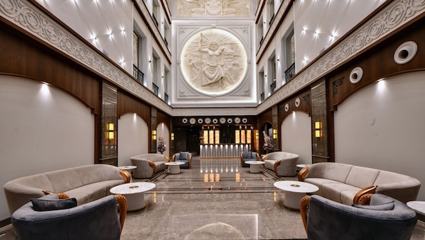 Um hall espaçoso com área de estar central, tetos altos com molduras decorativas e um imponente lustre.