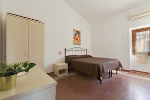 Quarto com cama, mesa de cabeceira e planta em vaso.