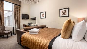 Quarto de hotel com uma cama grande, uma escrivaninha com um computador, uma cadeira e uma televisão na parede.