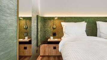 Quarto de hotel com uma cama grande, duas mesas de cabeceira com luminárias, um criado-mudo de madeira e uma cabeceira verde com textura.