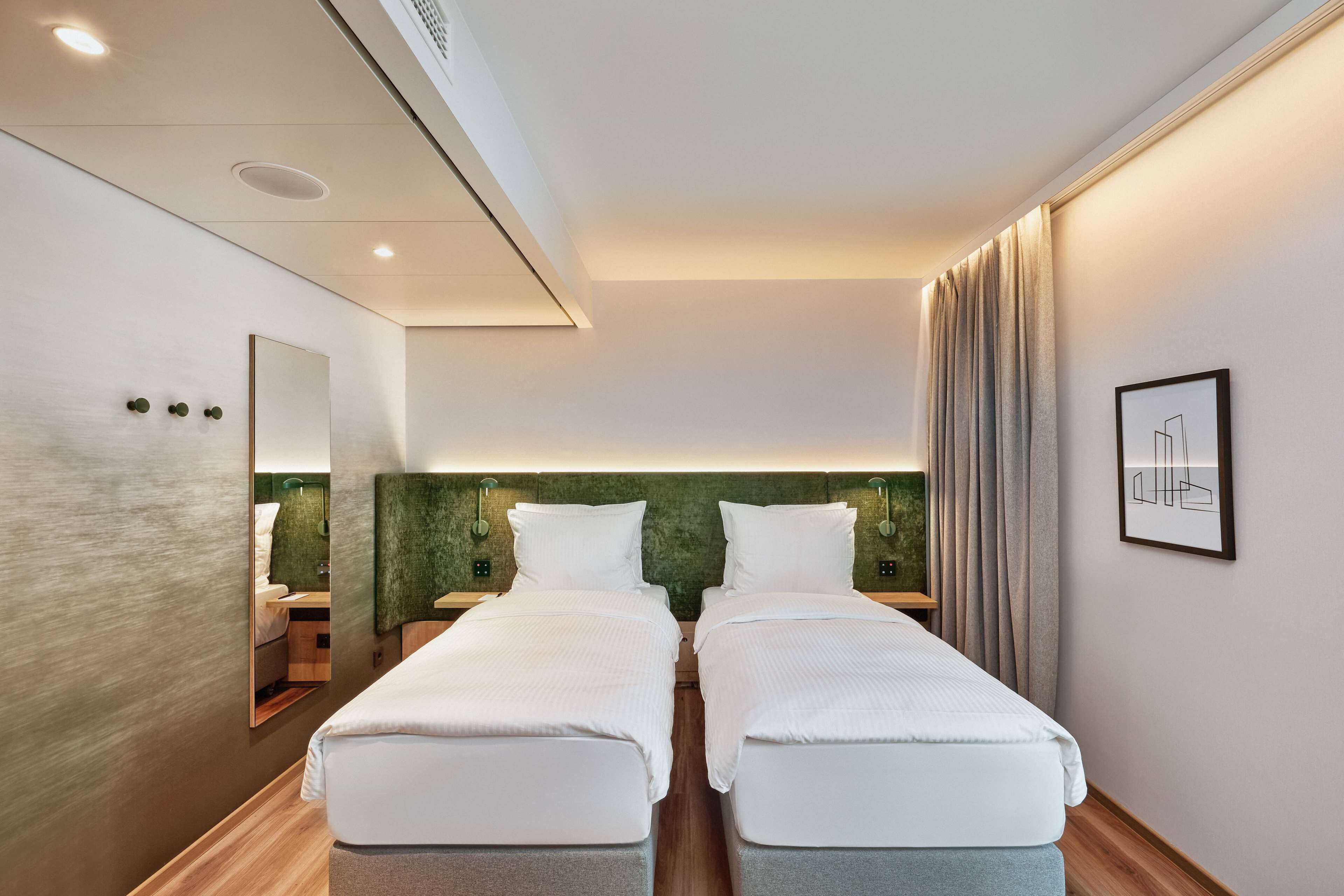 Quarto de hotel moderno com duas camas de solteiro, um espelho grande, uma parede texturizada verde e um quadro emoldurado na parede.