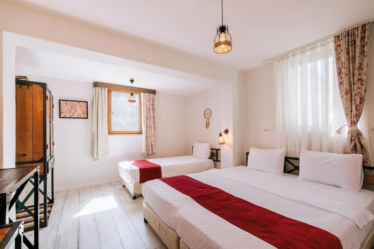 Quarto de hotel com duas camas, uma escrivaninha de madeira, uma janela com cortinas e um lustre.