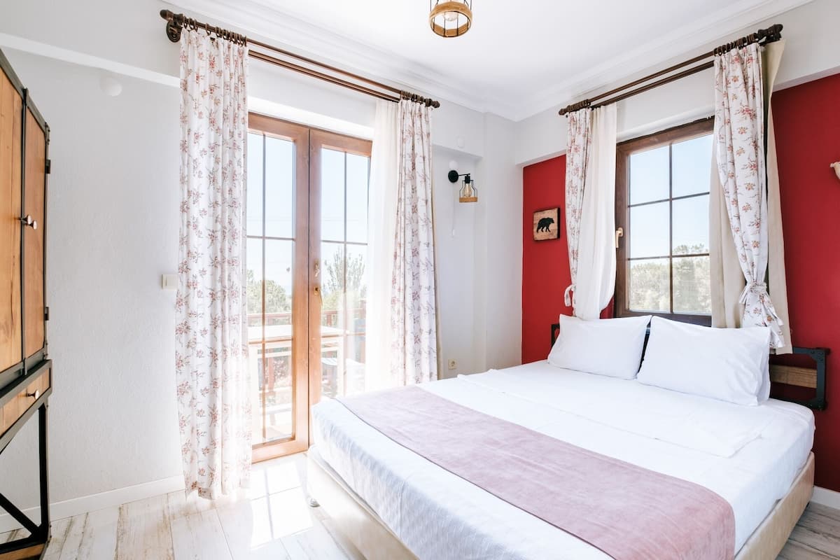 Quarto com cama, guarda-roupa de madeira, parede vermelha e janela com cortinas.