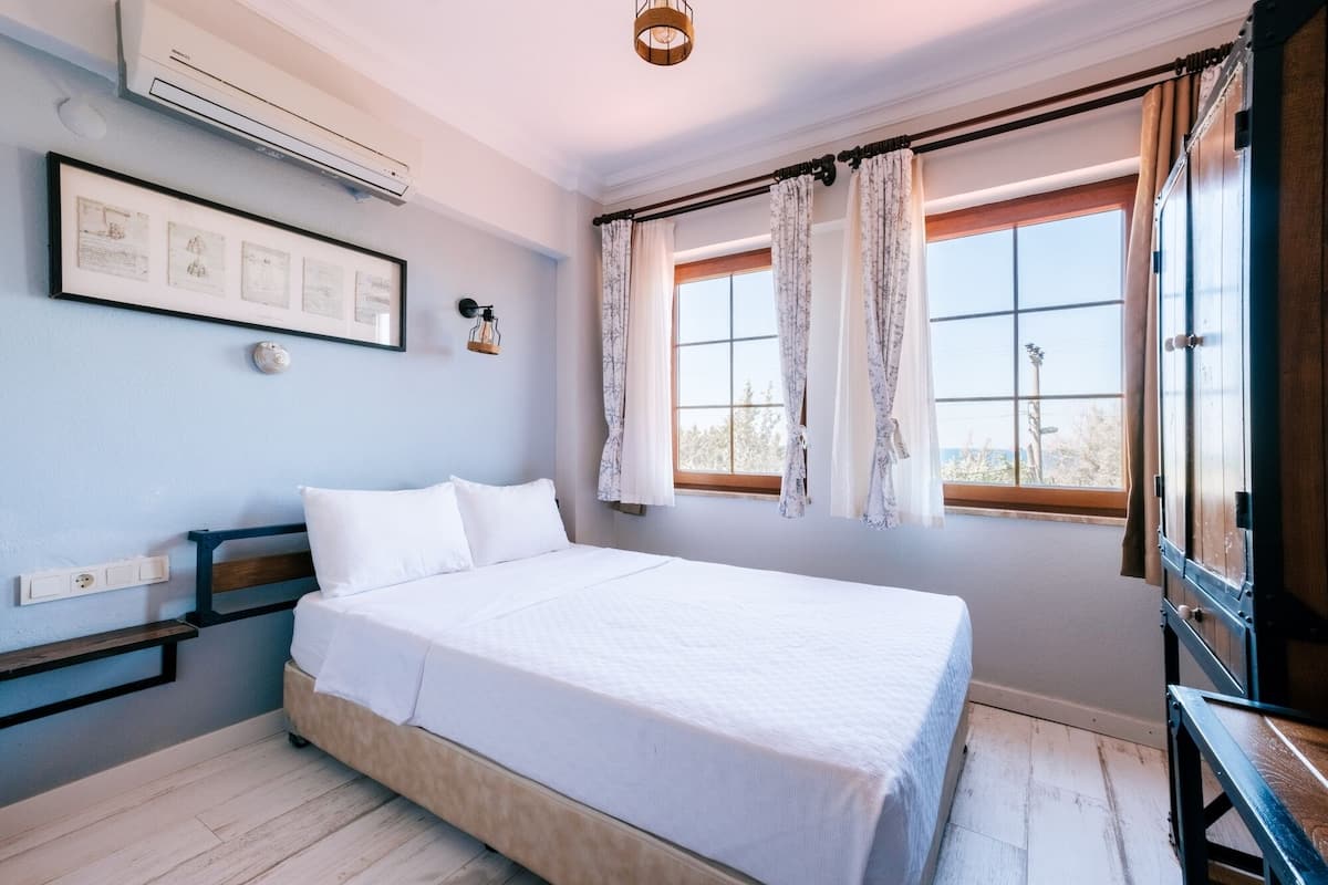 Quarto com cama, janela com cortinas, aparelho de ar condicionado e luminária na parede.