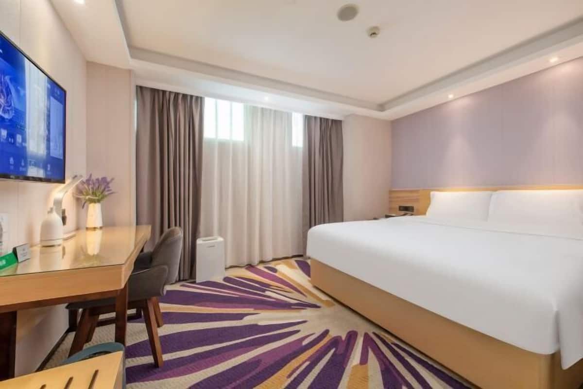 Quarto de hotel com cama, escrivaninha, cadeira, televisão e janela com cortinas.